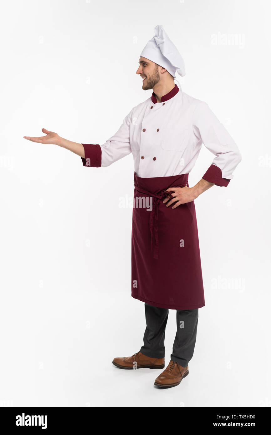 Full length of smiling young cook in uniform standing isolated over ...