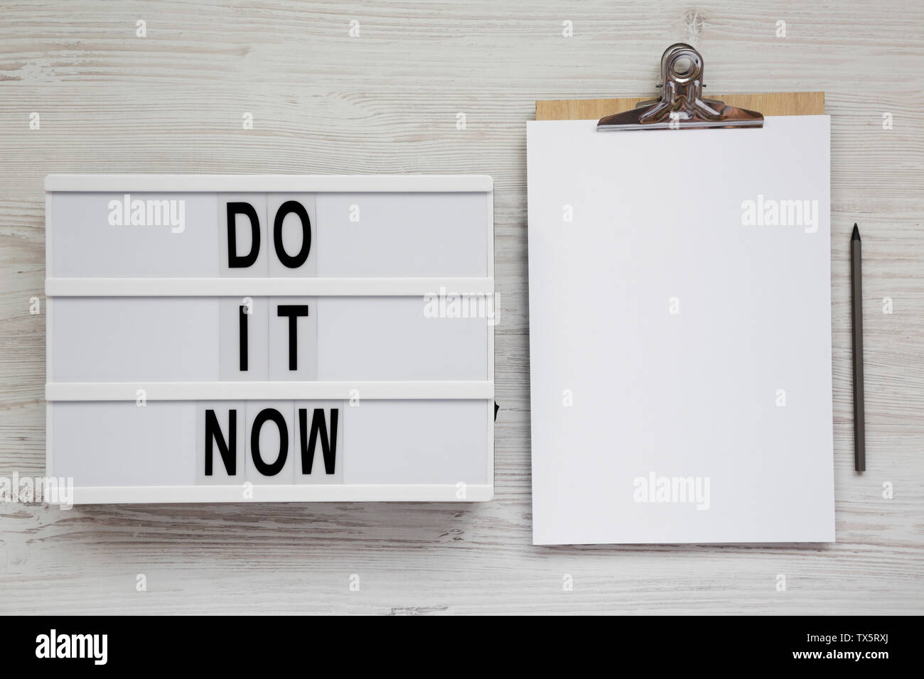 'Do it now' words on a lightbox, clipboard with blank sheet of paper on ...