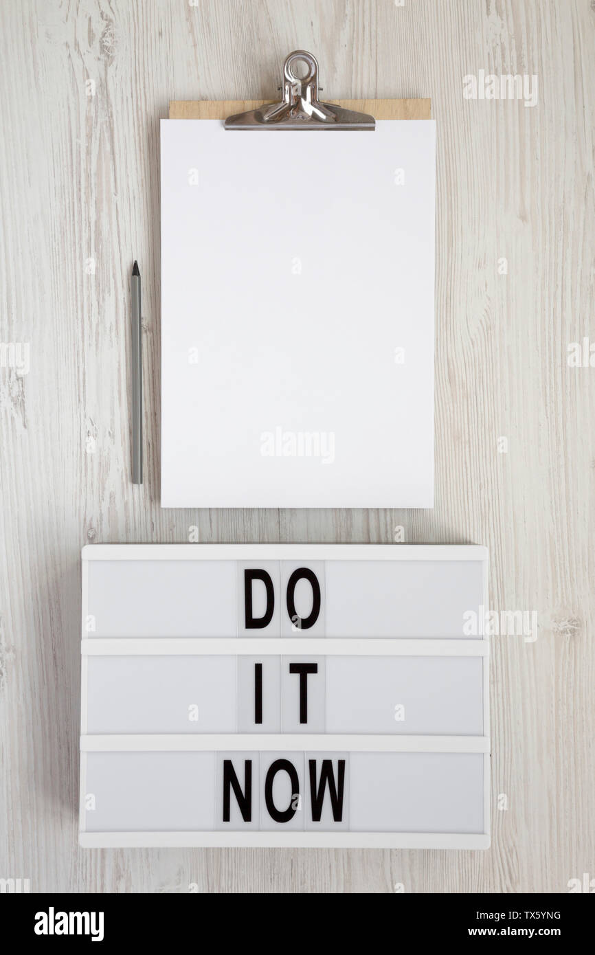 'Do it now' words on a lightbox, clipboard with blank sheet of paper on ...