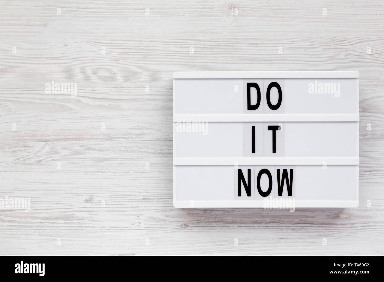 From above, 'Do it now' words on a modern board on a white wooden ...