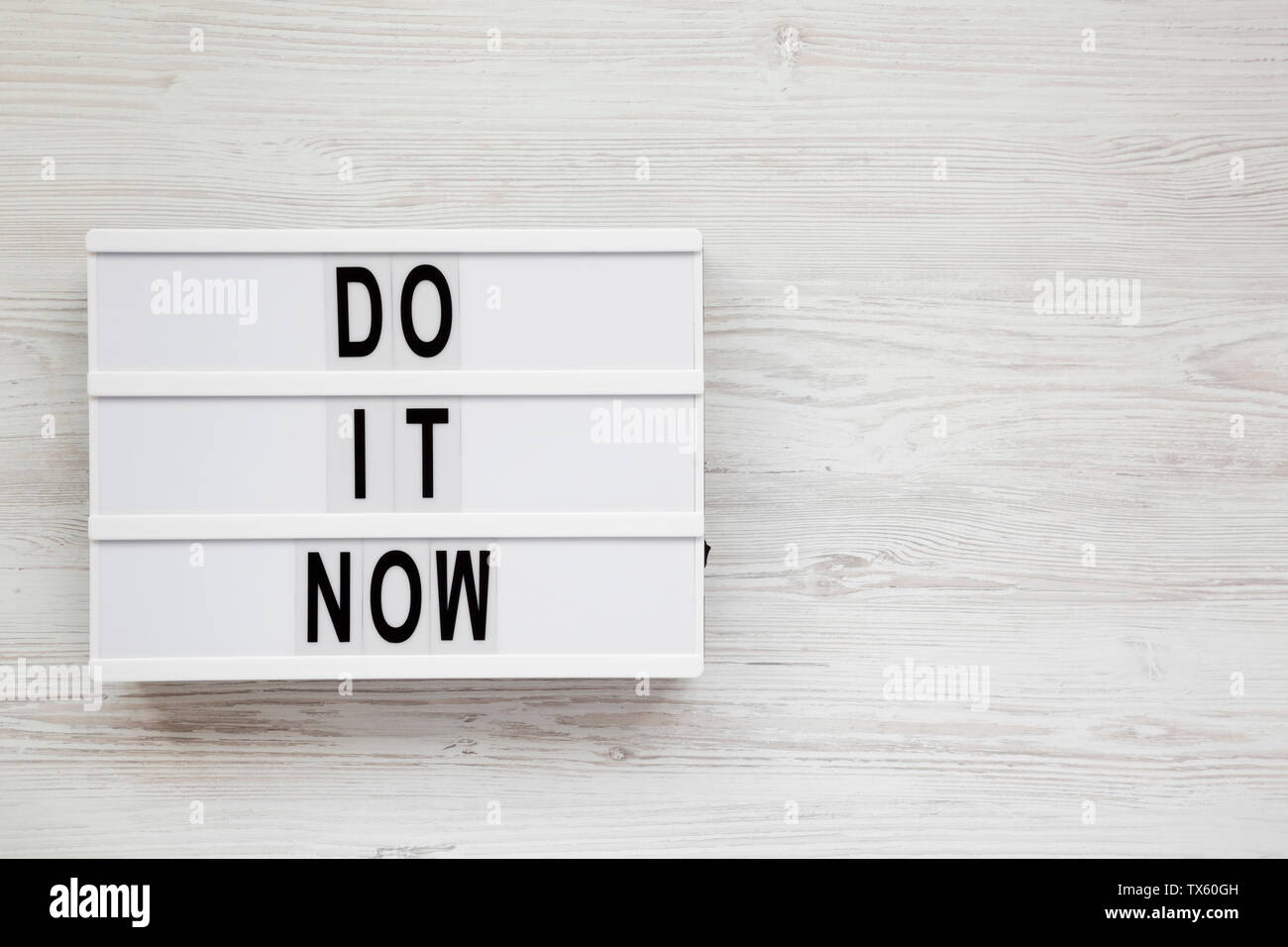 'Do it now' words on a lightbox on a white wooden background. Flat lay ...