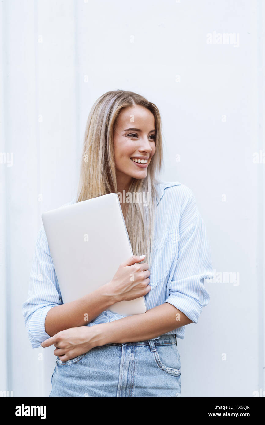 Beautiful smiling girl holding laptop computer while standing outdoors ...