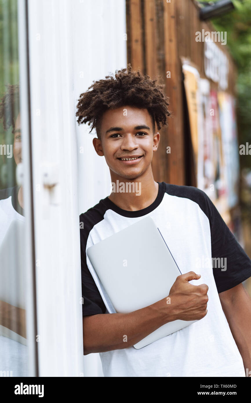 Happy african man student standing outdoors, carrying laptop computer ...