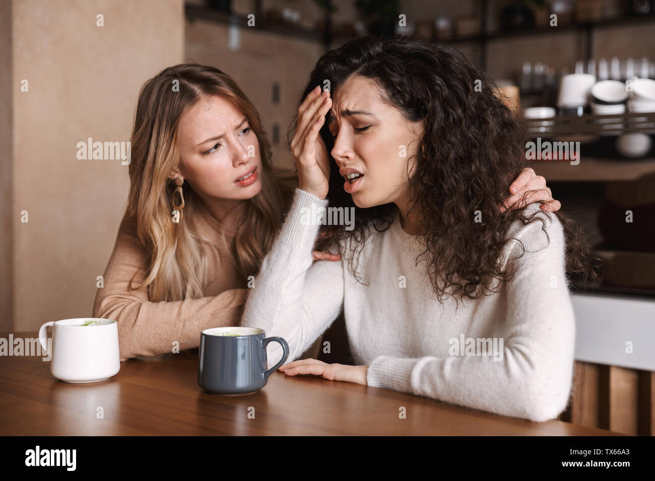 Two upset young girls friends sitting at the cafe table, drinking ...