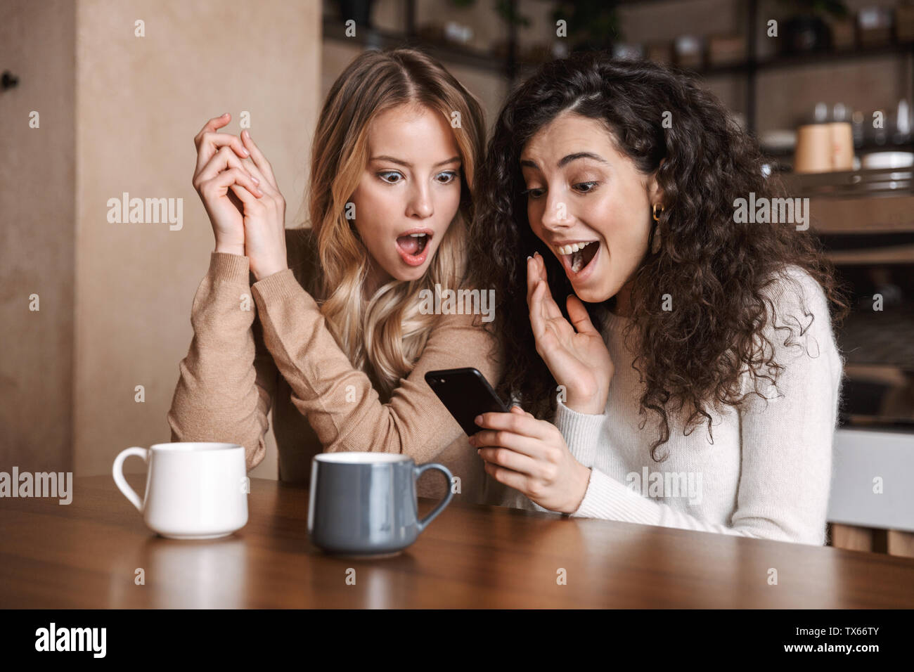 Image of excited emotional shocked girls friends sitting in cafe using ...