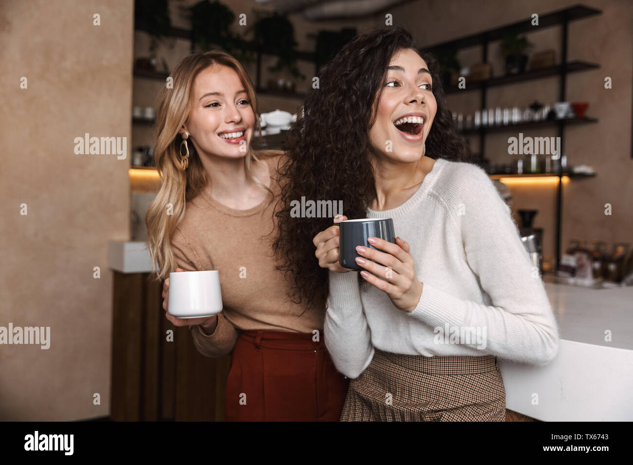 Two cheerful young girls friends standing at the cafe counter, having ...