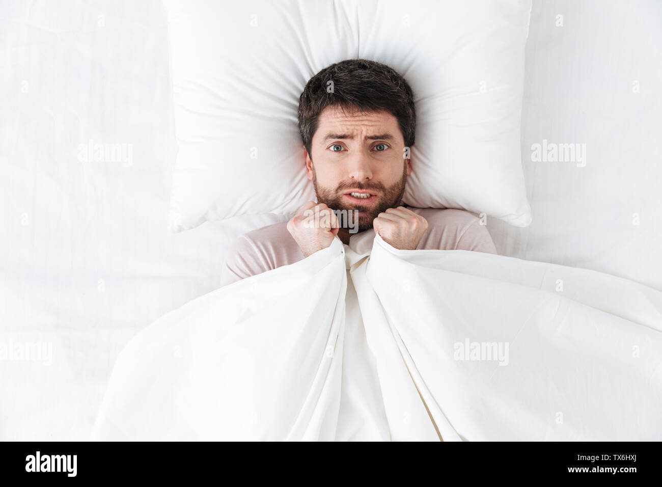 Image of a scared handsome young man in the morning under blanket hide ...
