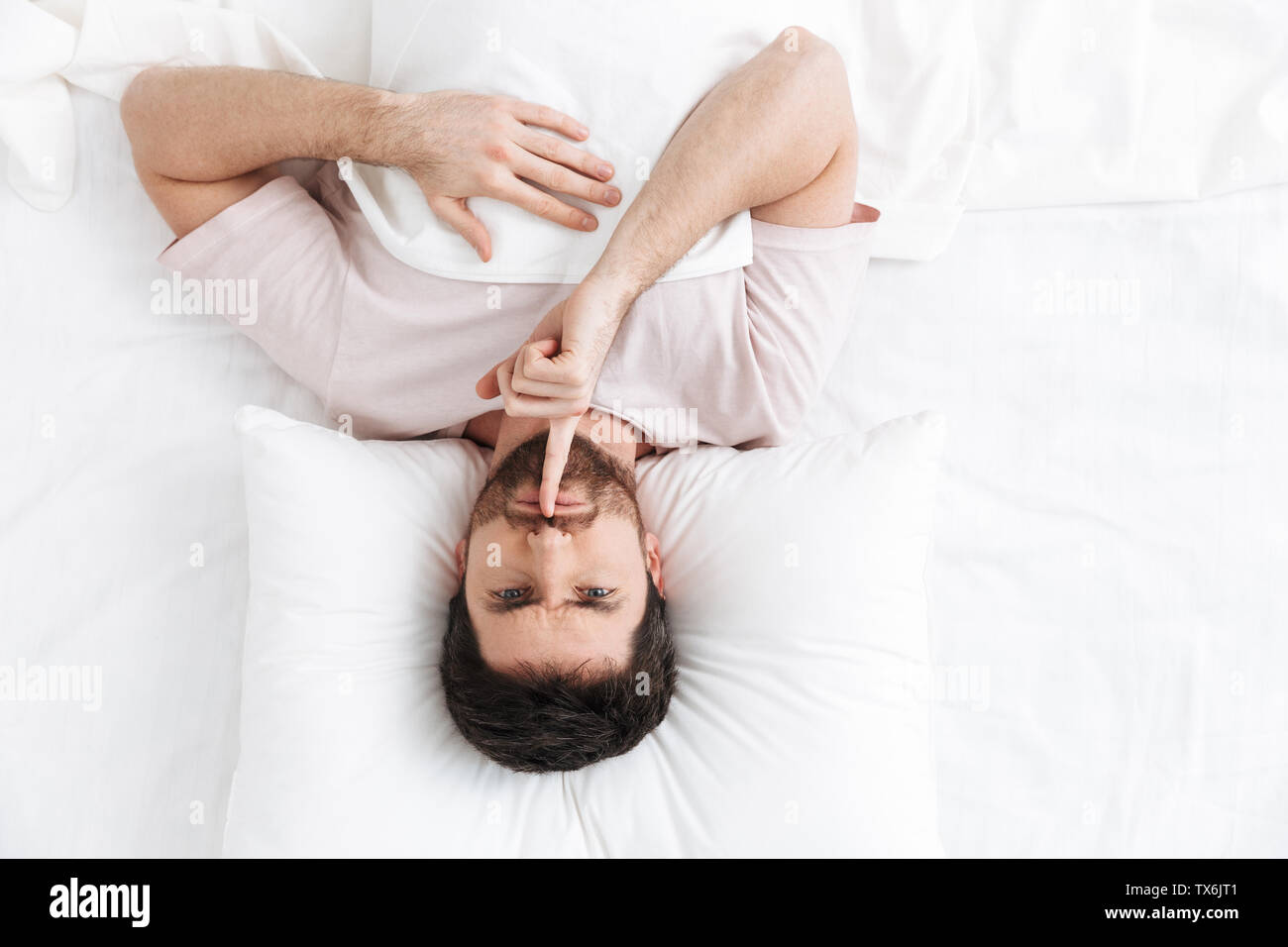 Top view of a handsome young man laying in bed, showing silence gesture ...