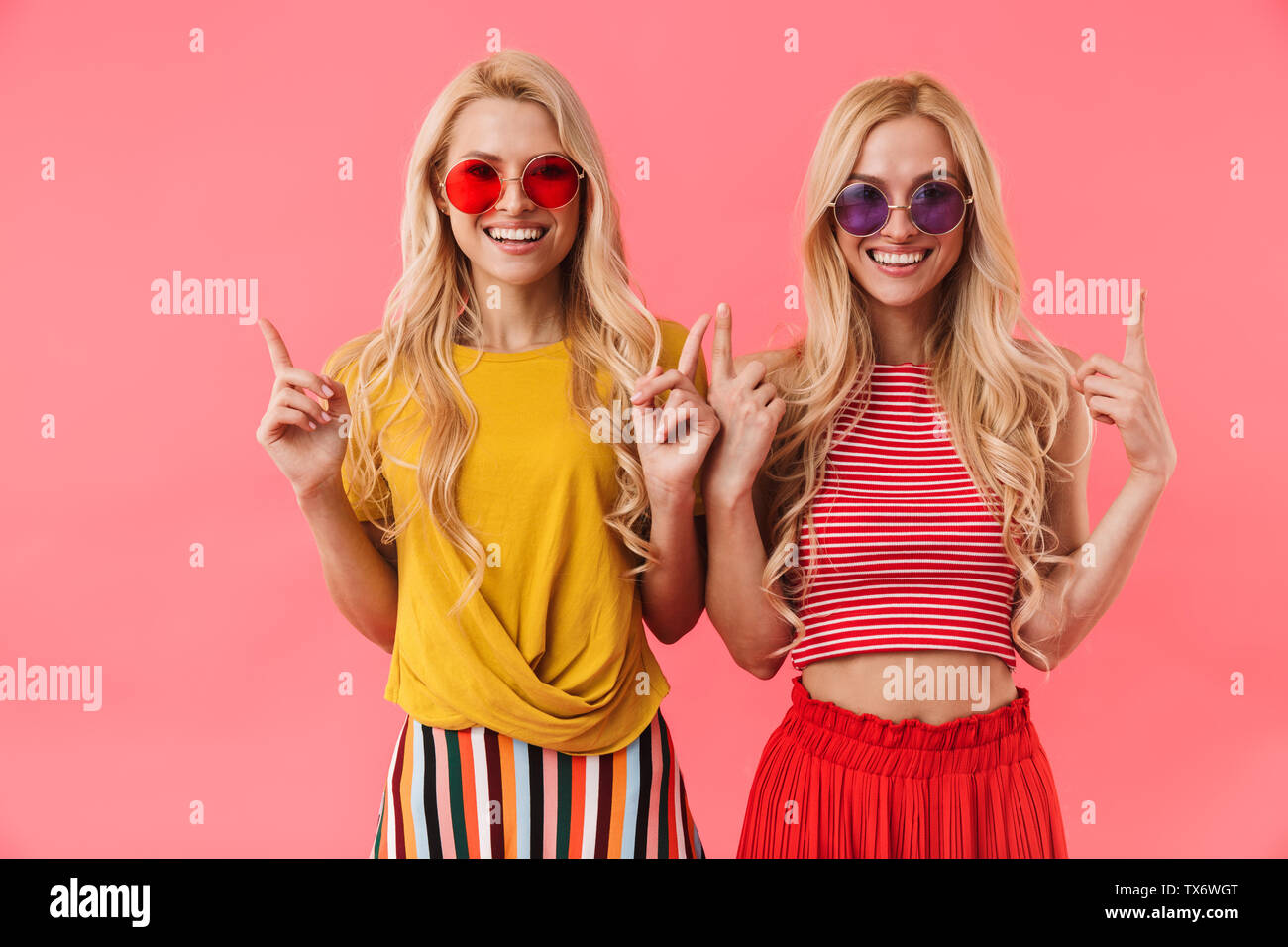 Smiling blonde twins in sunglasses pointing up and looking at the ...