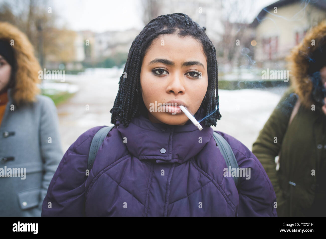 young african woman posing outdoor in the street and smoking cigarette ...