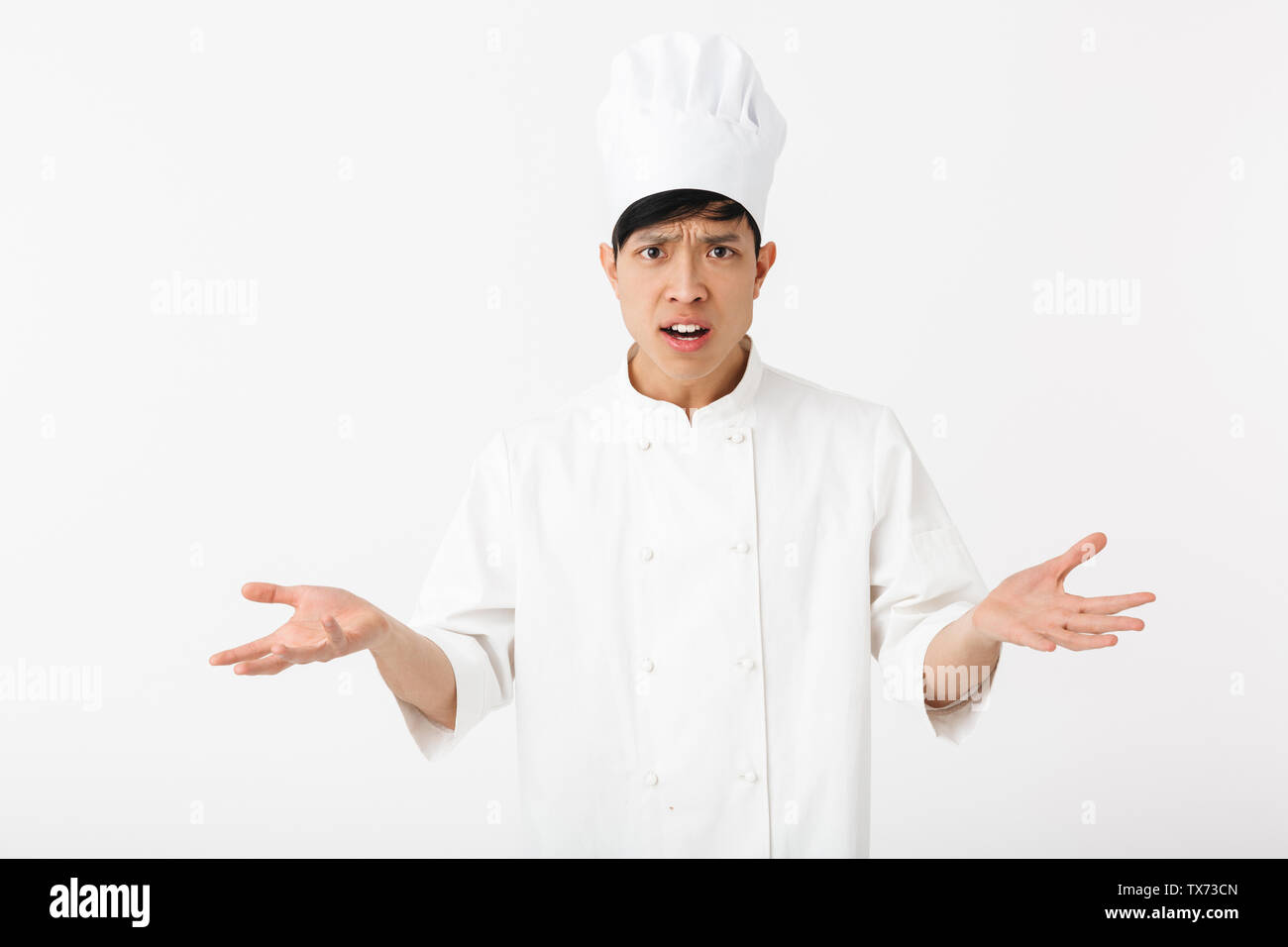 Confused asian chef wearing uniform standing isolated over white ...