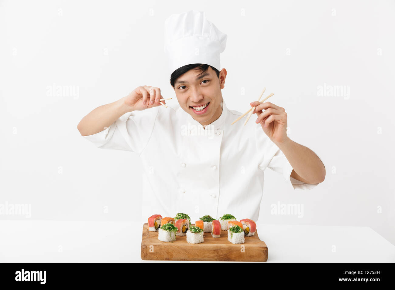 Image of pleased chinese chief man in white cook uniform eating sushi ...