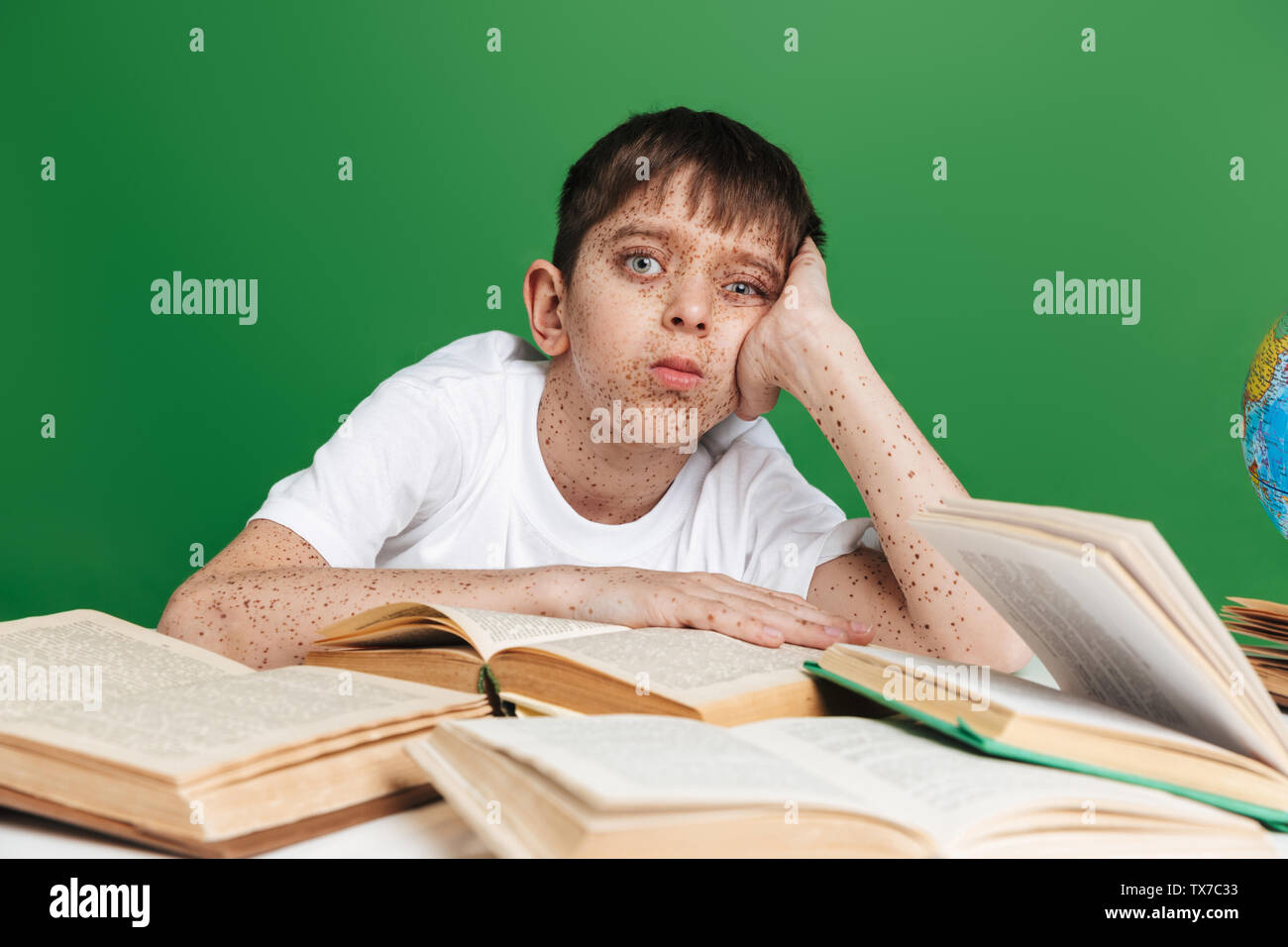 Cute confused little boy with freckles studying, sitting with stack of ...