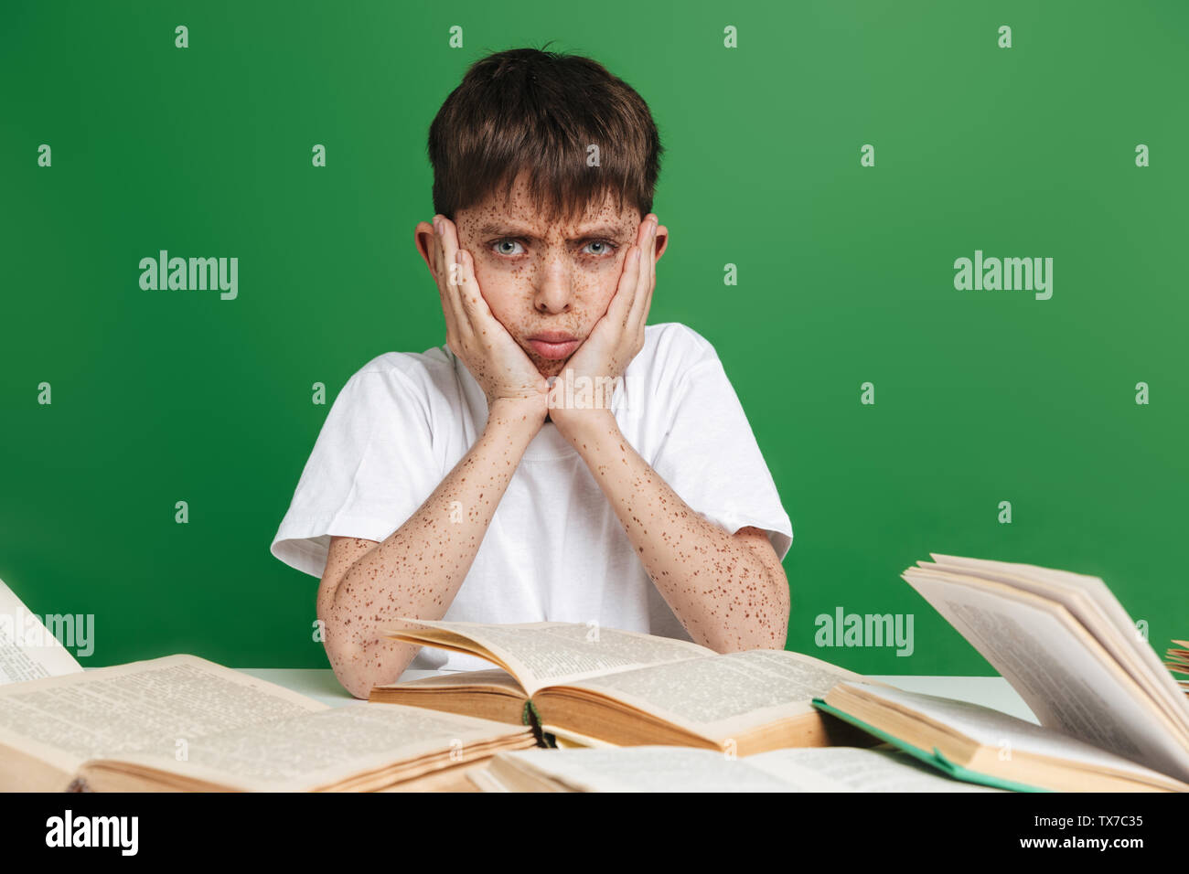 Cute confused little boy with freckles studying, sitting with stack of ...