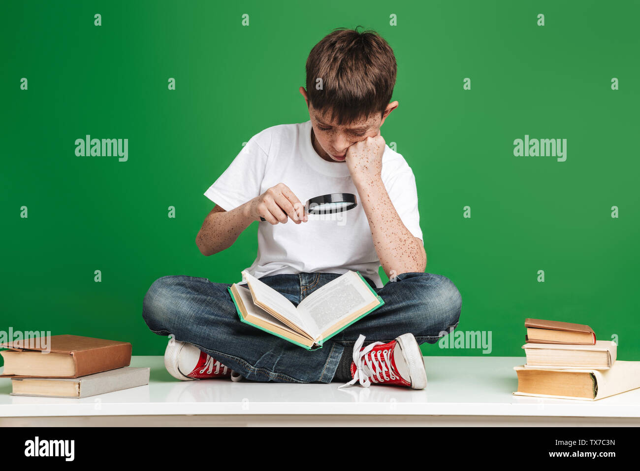 Cute confused little boy with freckles studying, sitting with stack of ...