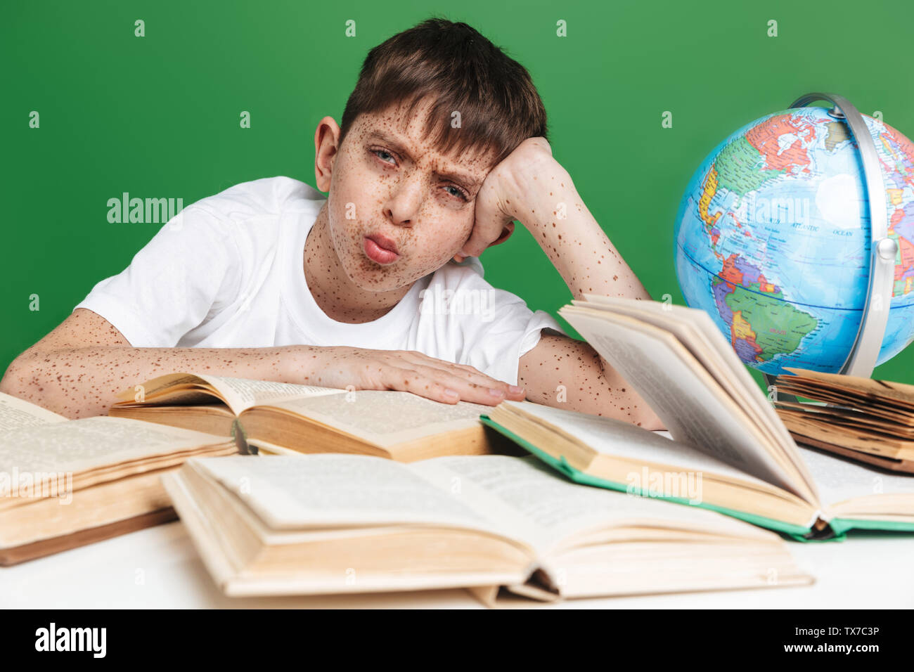 Cute confused little boy with freckles studying, sitting with stack of ...