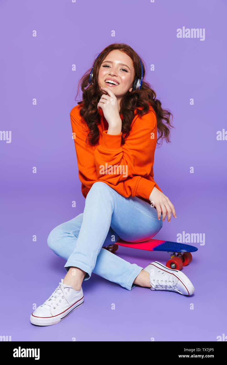 Portrait of a pretty young redheaded woman sitting on skateboard ...