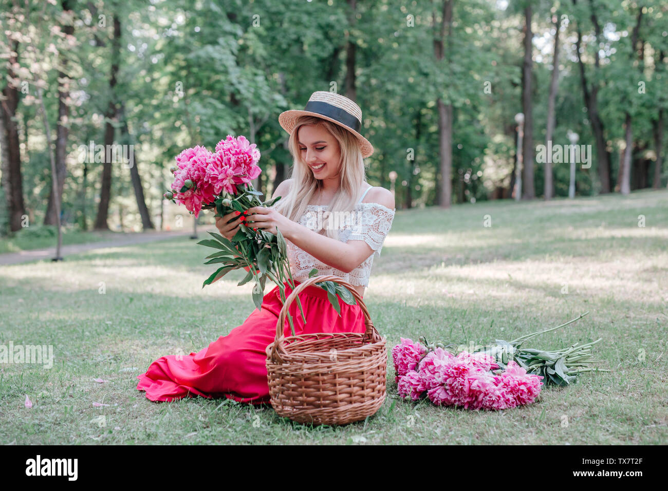 Romantic woman florist in straw hat makes a bouquet with pink peonies ...