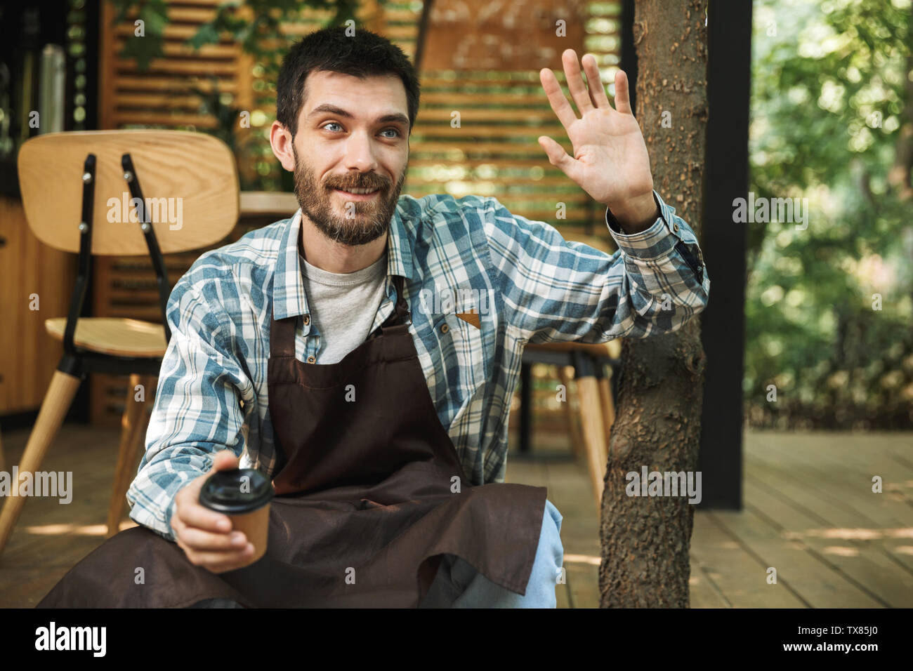 Photo of friendly waiter man wearing apron sitting on wooden floor ...