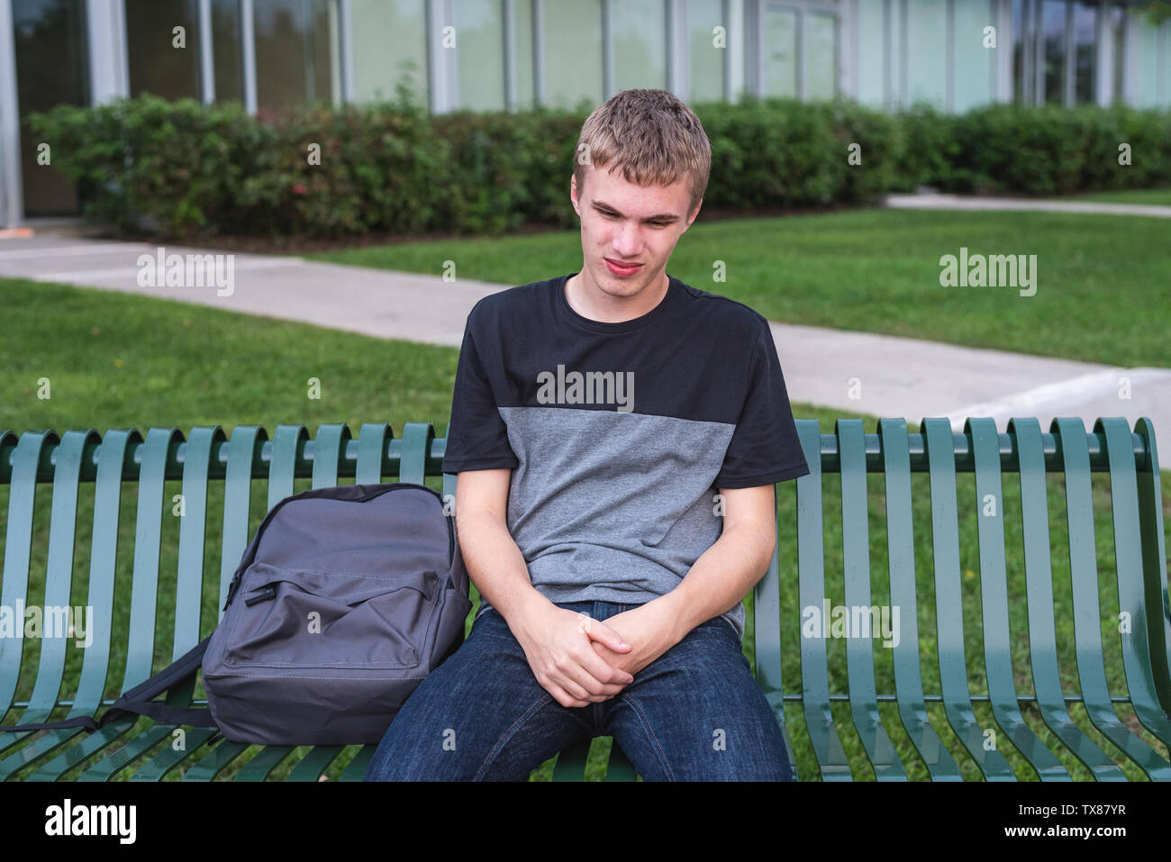 Lonely teenager sitting on a bench outside of his high school Stock ...