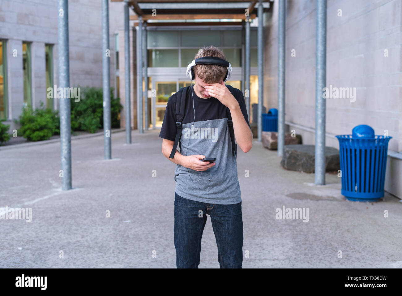 Confused male teenager standing in front of his school while listening ...