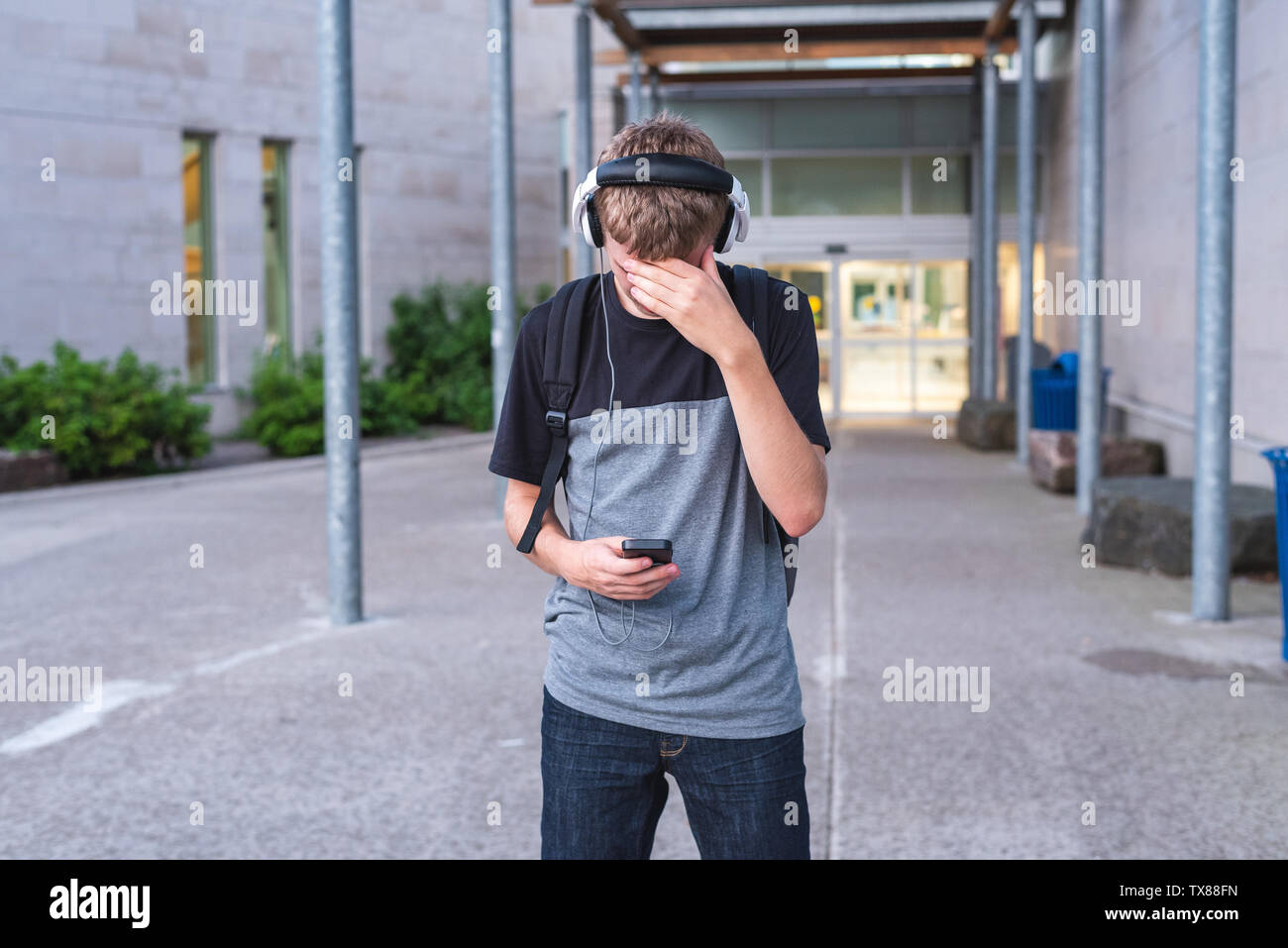 Confused male teenager standing in front of his school while listening ...