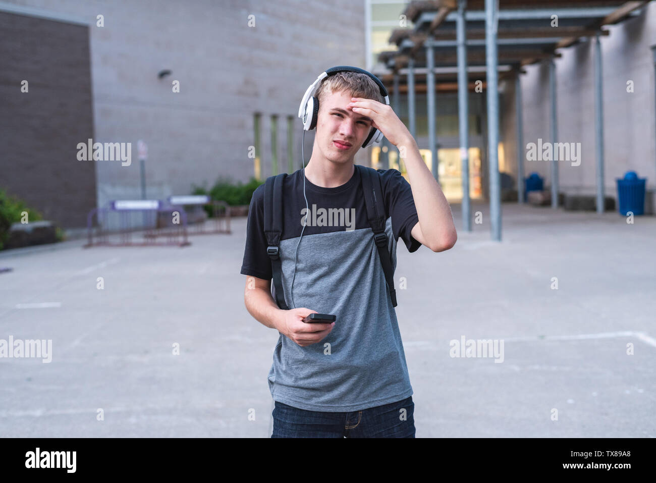 Confused male teenager standing in front of his school while listening ...