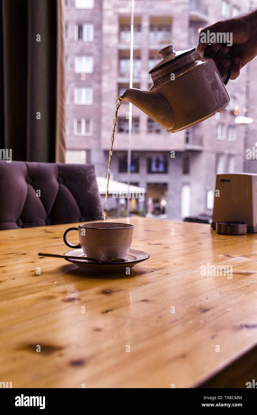 Fresh tea being poured into a tea cup from a ceramic tea pot on a ...