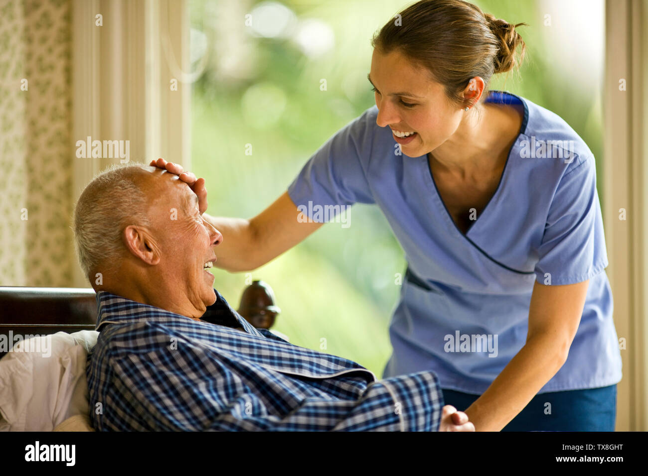 Female nurse leans over to place a hand on the forehead of a senior man ...