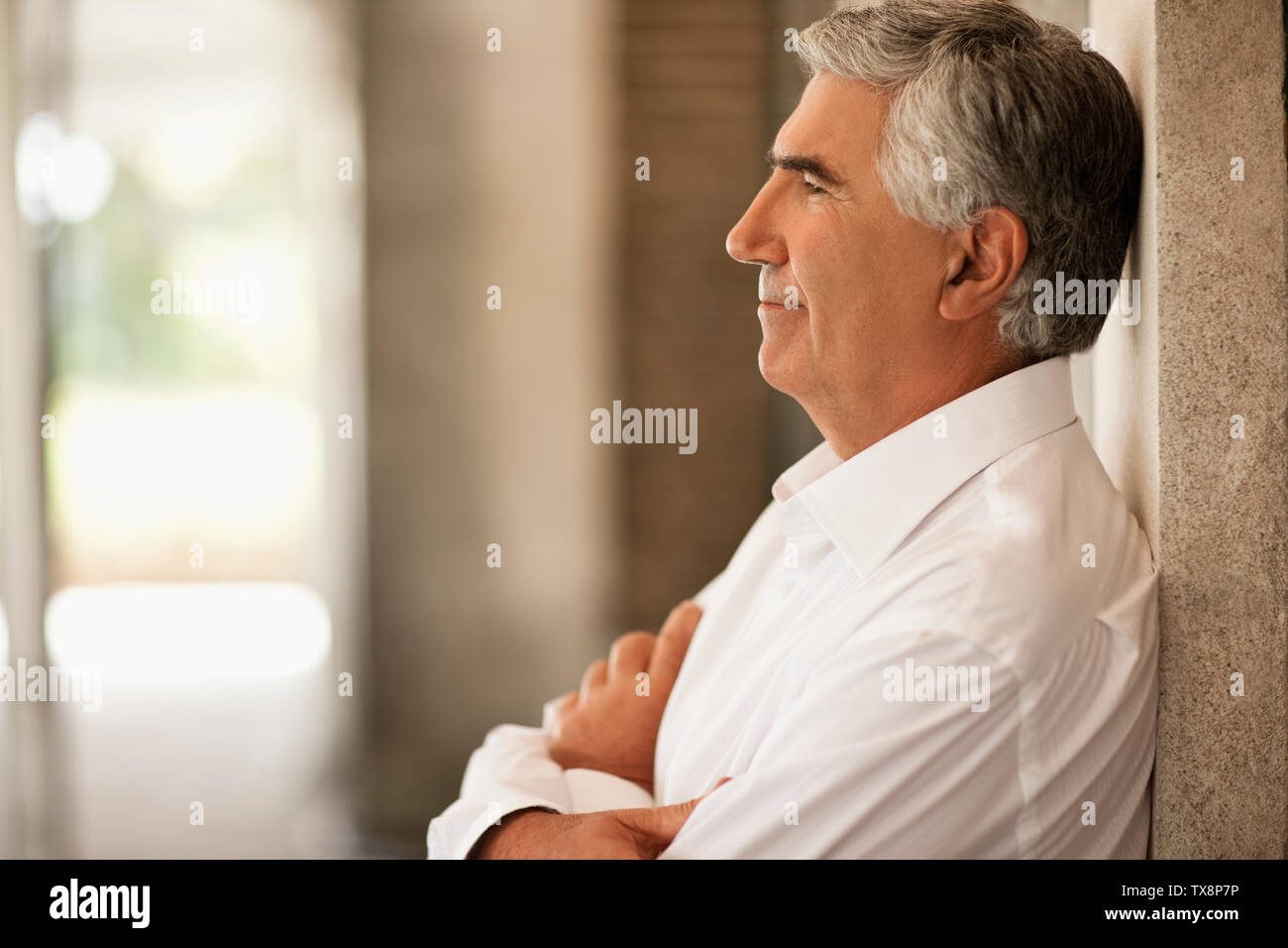 Side view of mature man leaning against wall with arms folded Stock ...