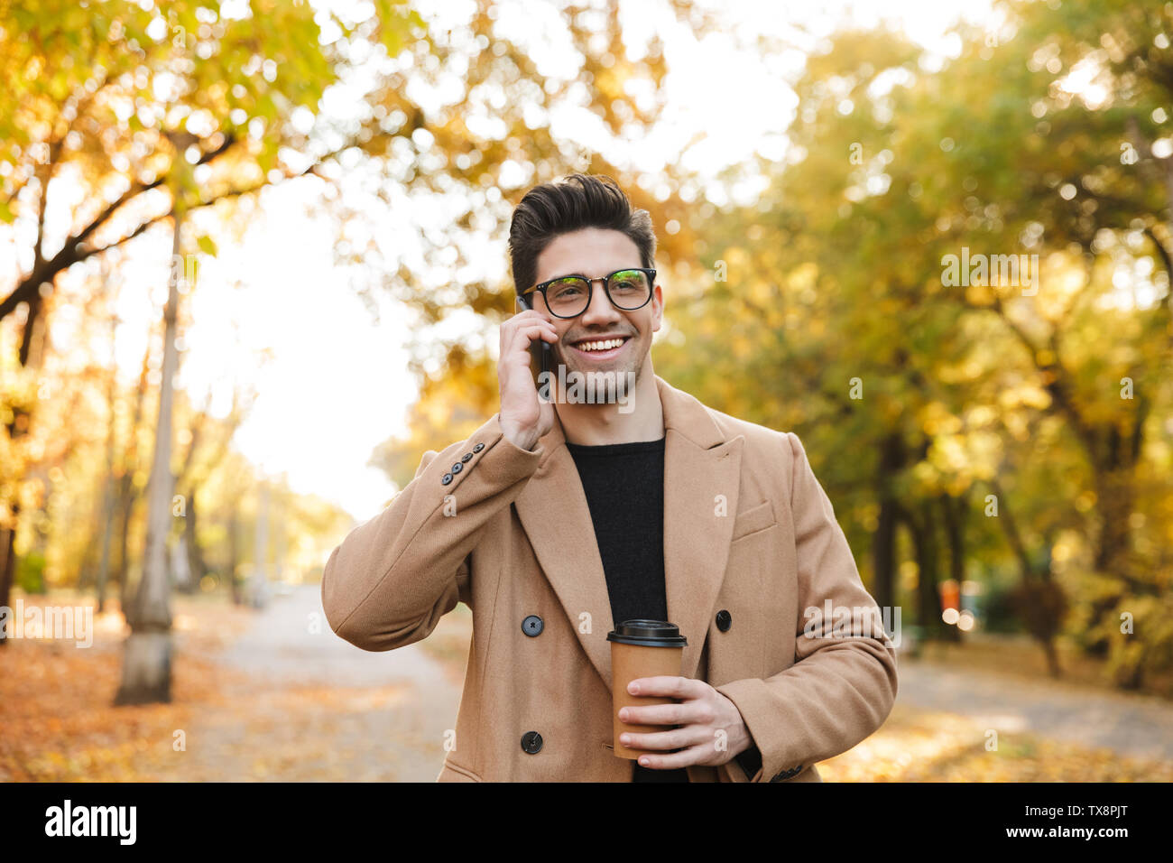 Image of handsome young man wearing coat talking on smartphone and ...