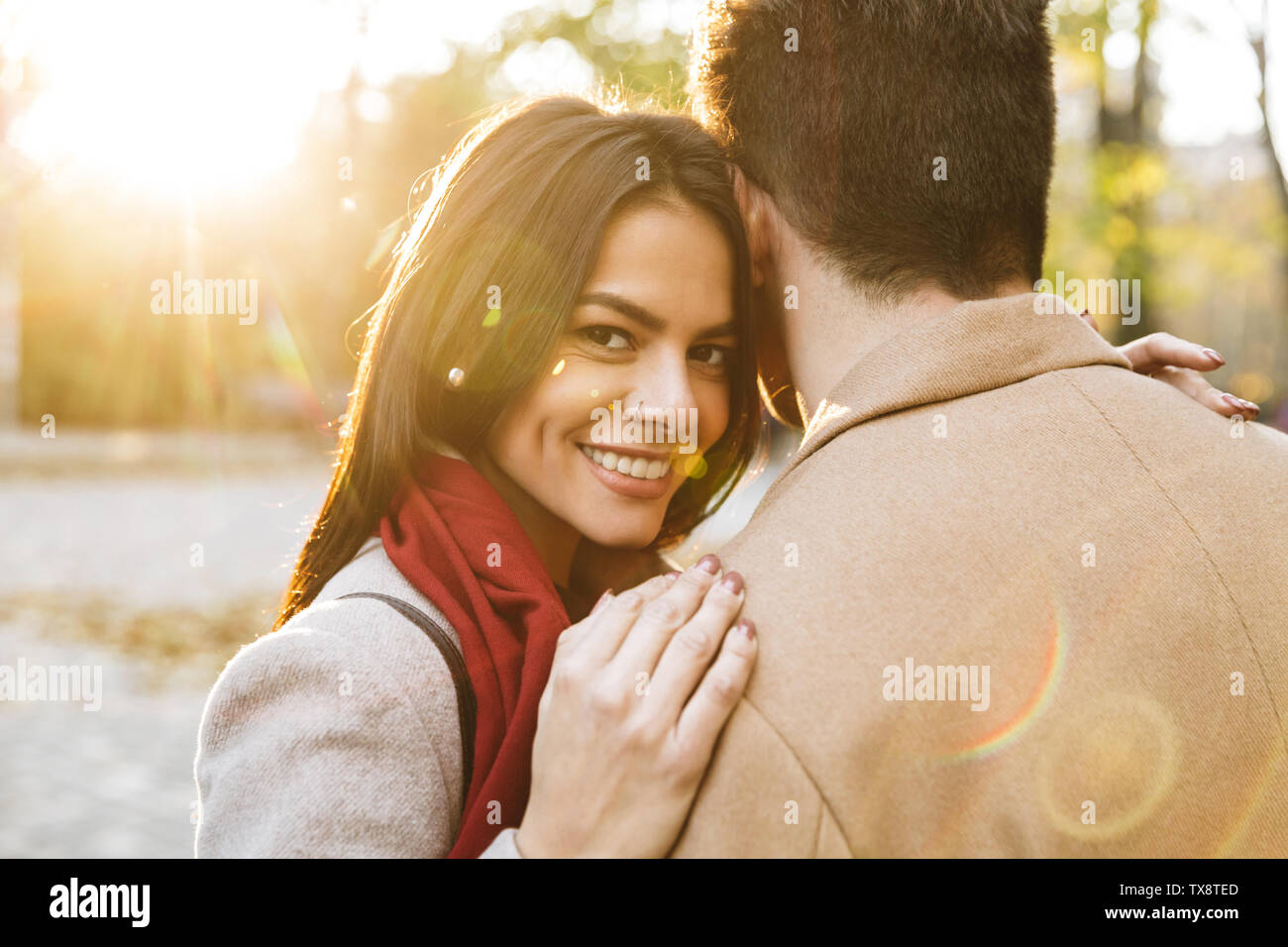 Image of young beautiful woman hugging her boyfriend and smiling while walking in autumn park ...