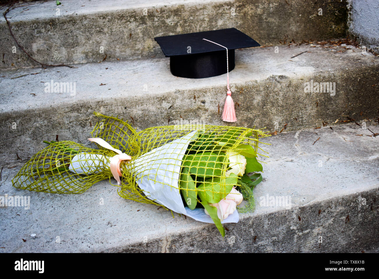Graduation cap or mortaboard with a bunch of roses on the old stairs in ...