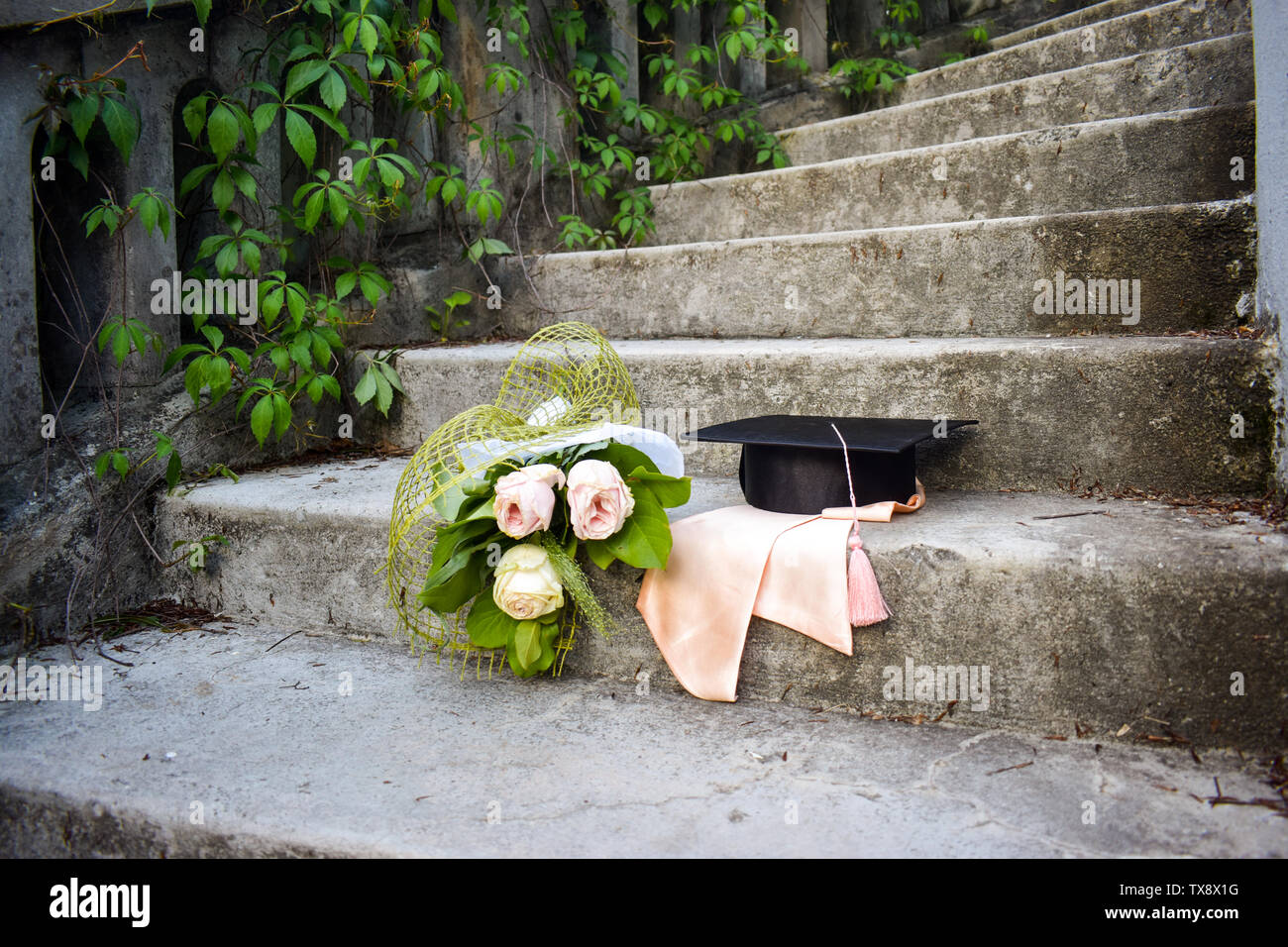 Graduation cap or mortaboard with a bunch of roses on the old stairs in ...