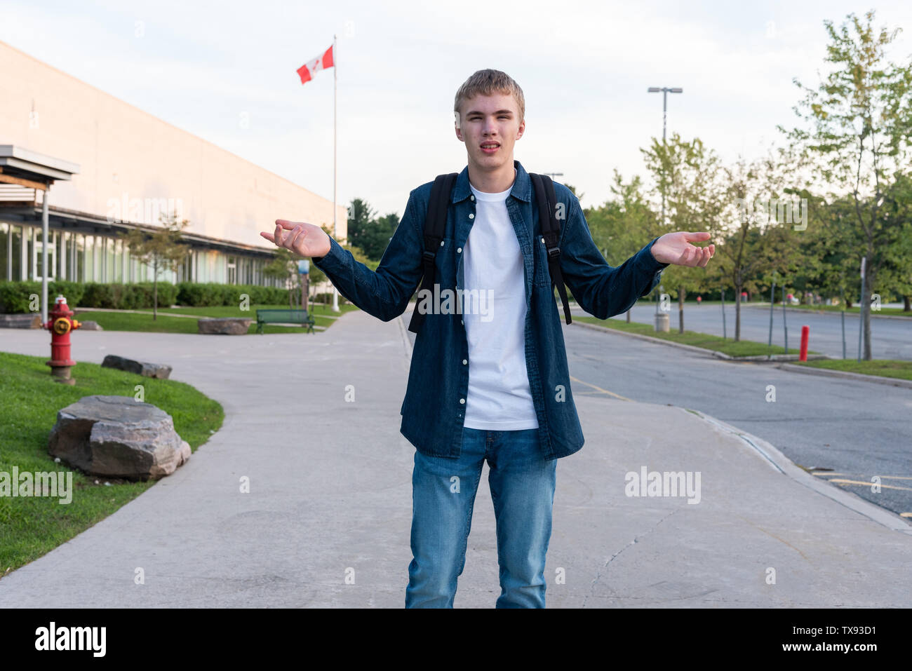 Confused teenager standing on a sidewalk with a high school in the ...