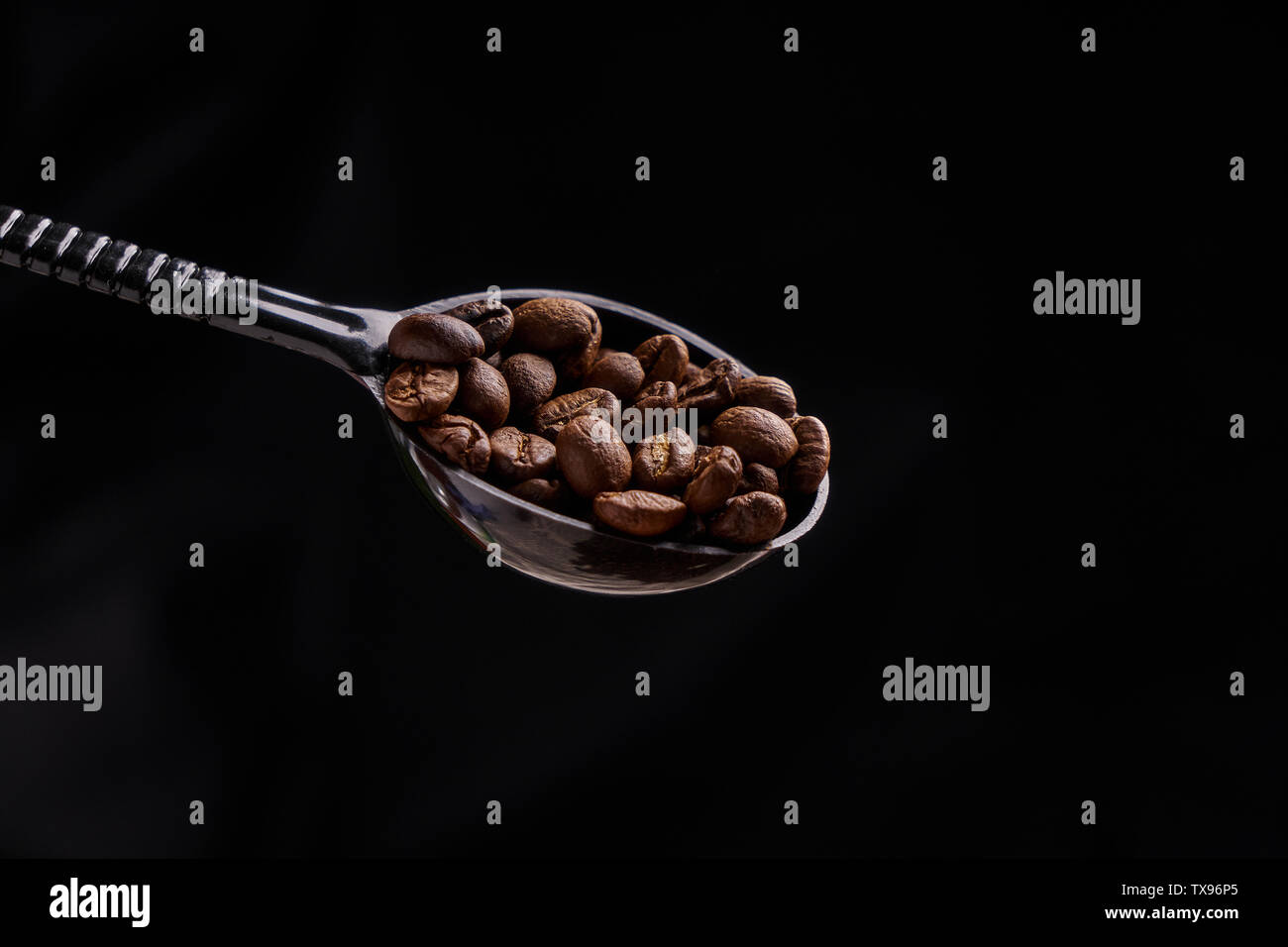 A spoonful of coffee beans in a black background Stock Photo - Alamy