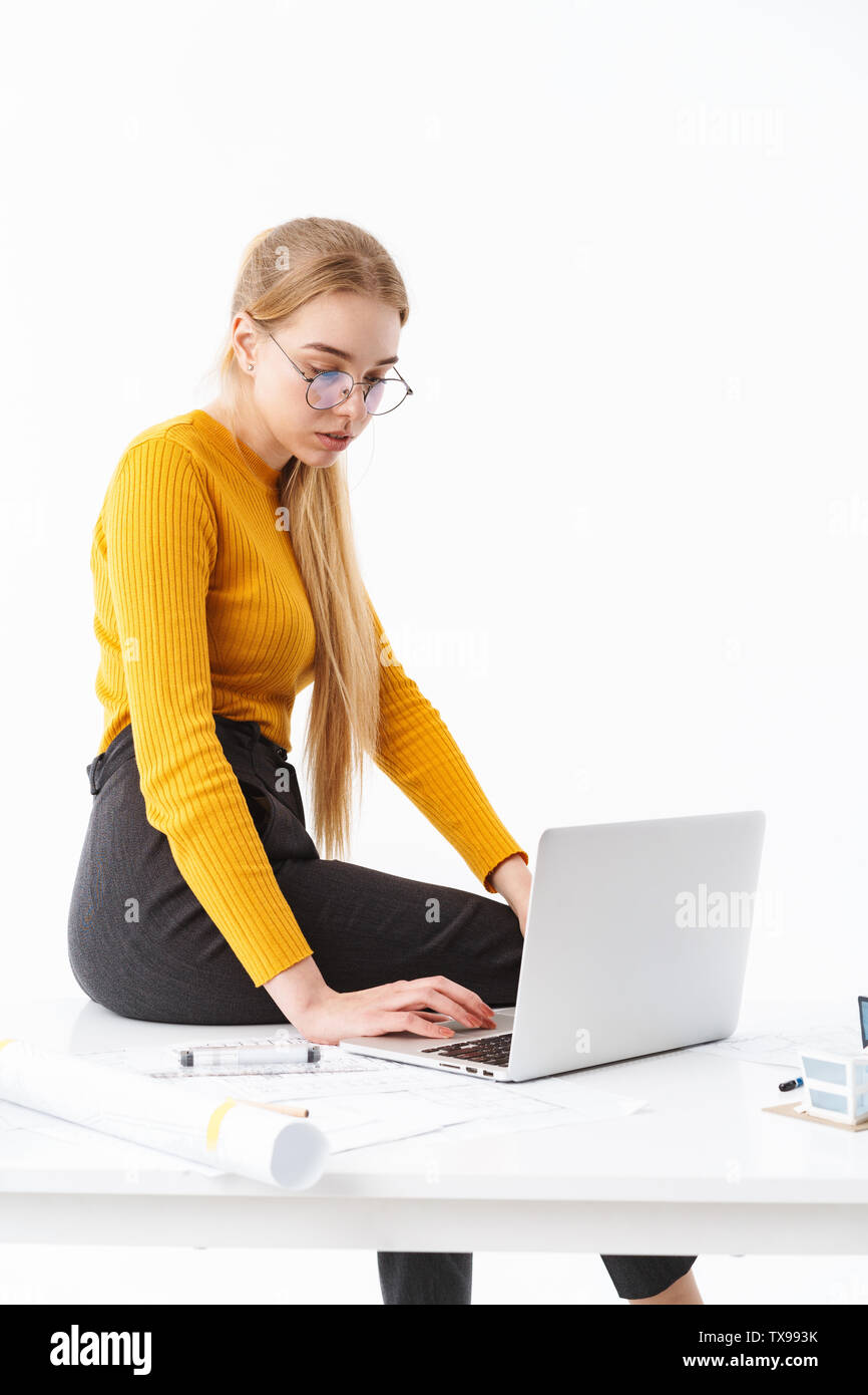 Beautiful young woman sitting on the desk, working on laptop computer ...