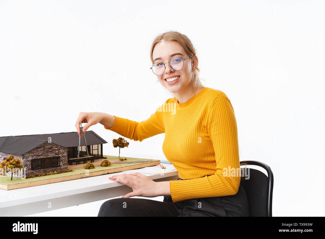 Lovely young woman architect sitting at the desk with house model ...