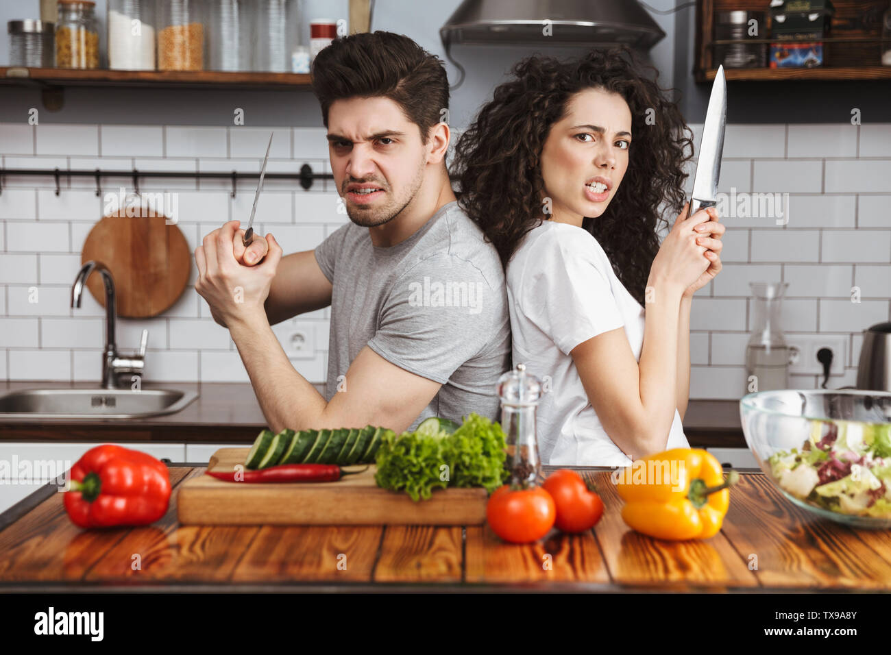 Excited angry young couple cooking healthy salad while sitting at the ...