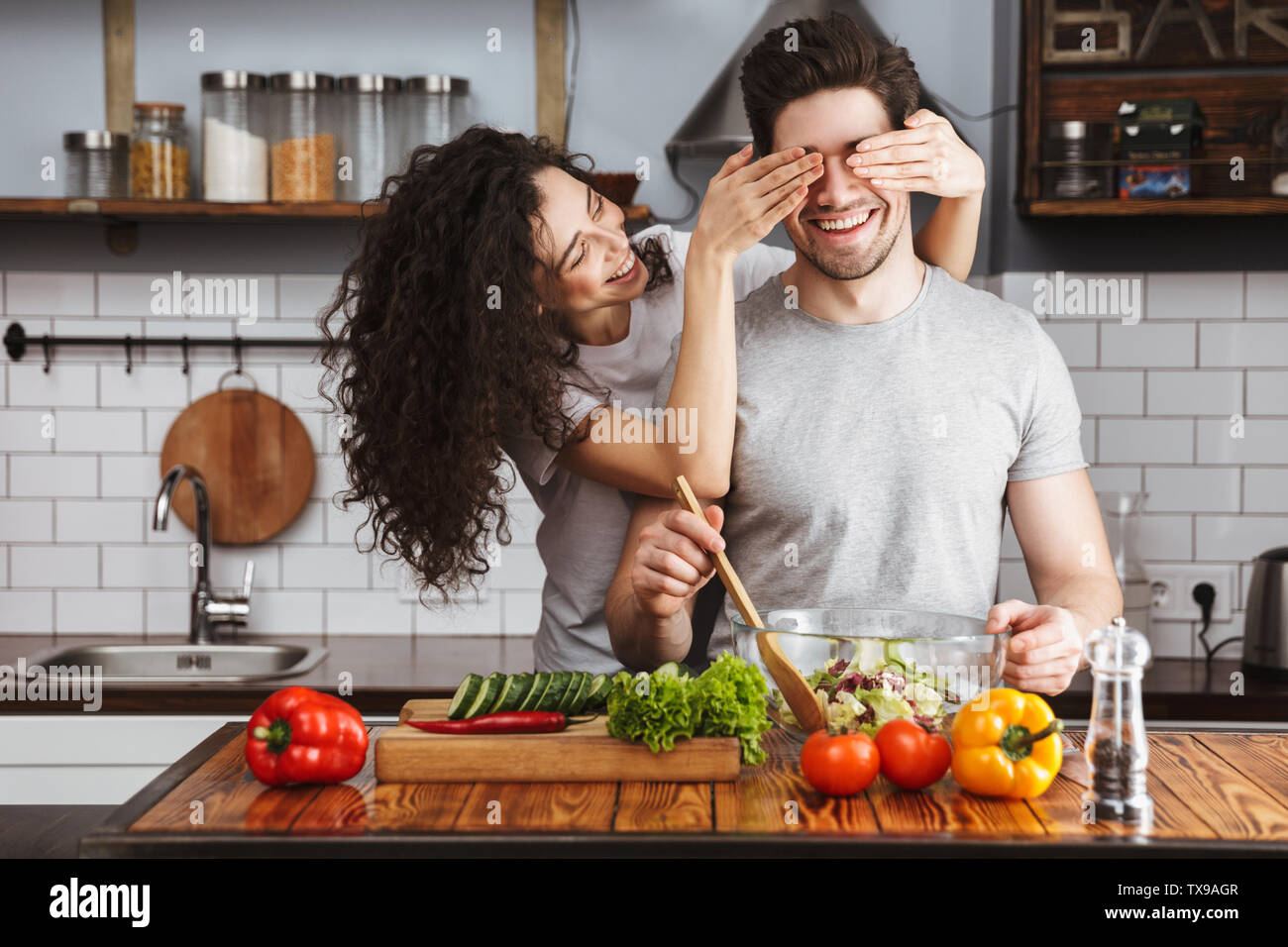 Excited cheerful young couple cooking healthy salad while sitting at ...