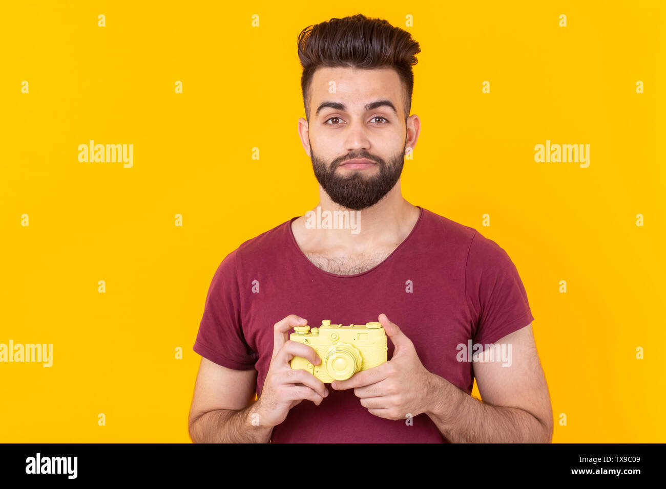 Positive young hipster man with a beard holding a yellow vintage camera ...
