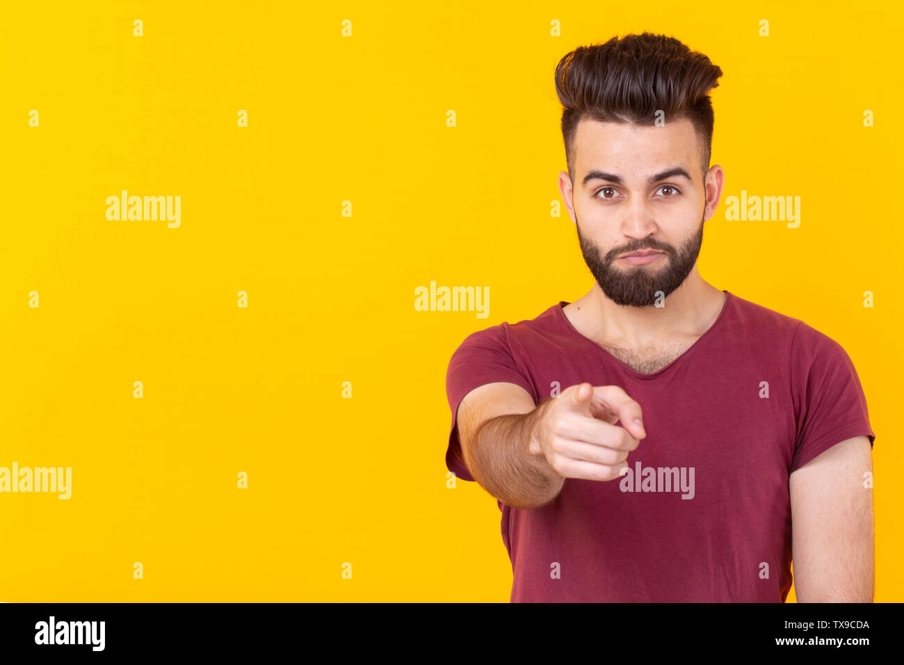Cute young hipster man with a beard pointing at the camera is posing on ...