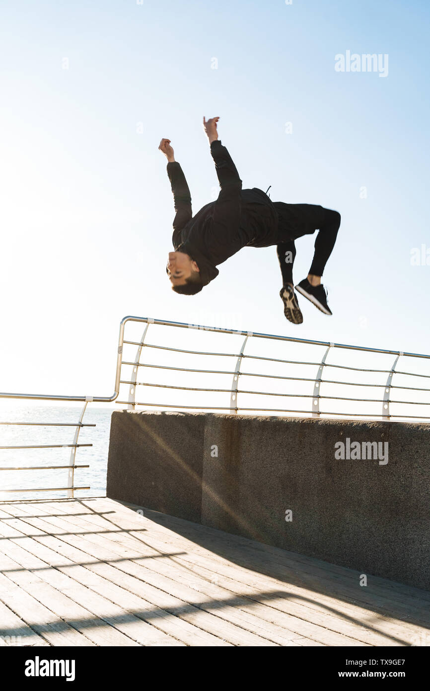 Photo of athletic man 20s in black tracksuit doing acrobatics and ...