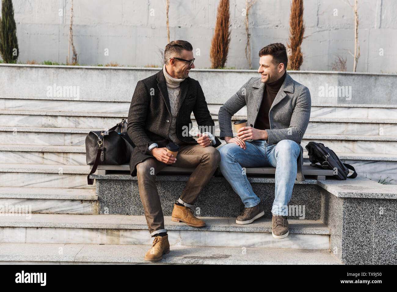 Two handsome men wearing coats spending time outdoors, drinking ...
