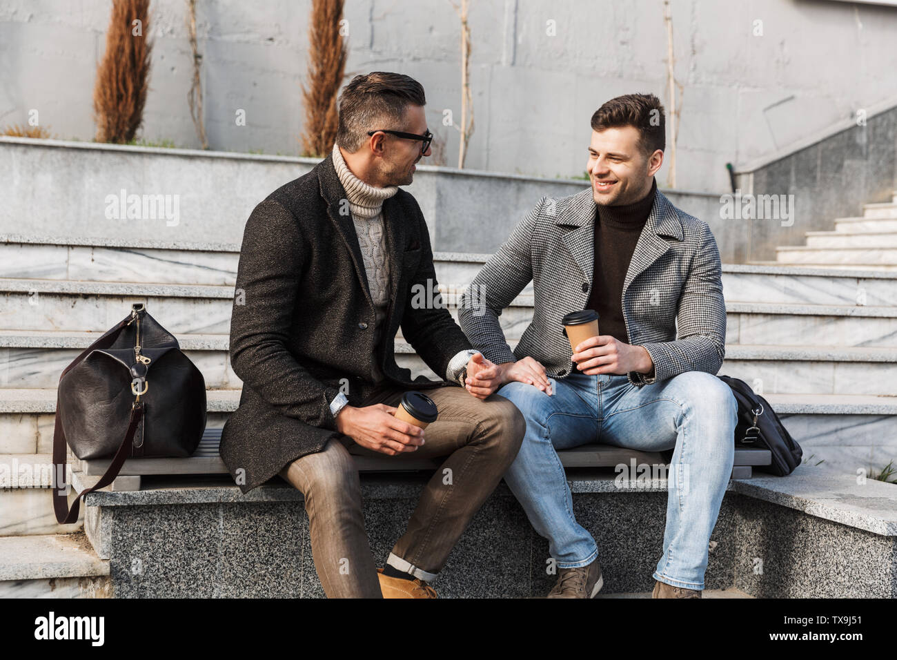 Two handsome men wearing coats spending time outdoors, drinking ...