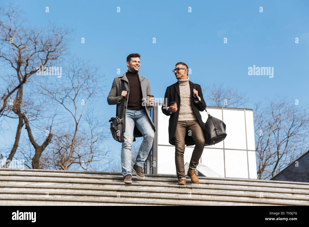 Two handsome men wearing coats spending time outdoors, drinking ...