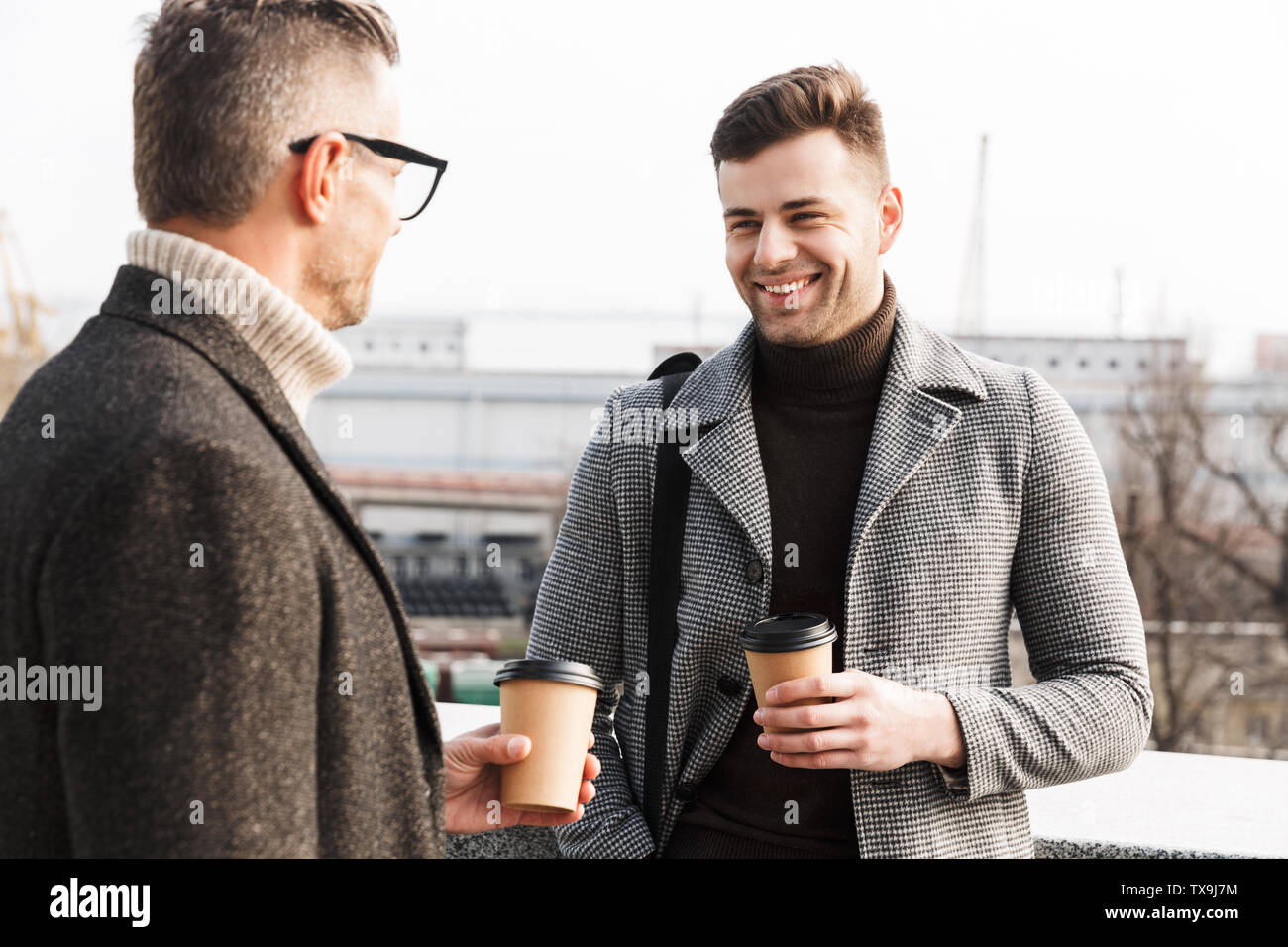 Two handsome men wearing coats spending time outdoors, drinking ...