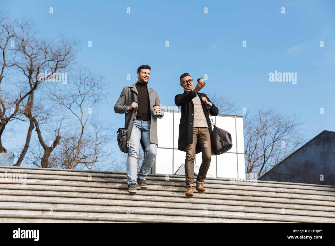 Two handsome men wearing coats spending time outdoors, drinking ...
