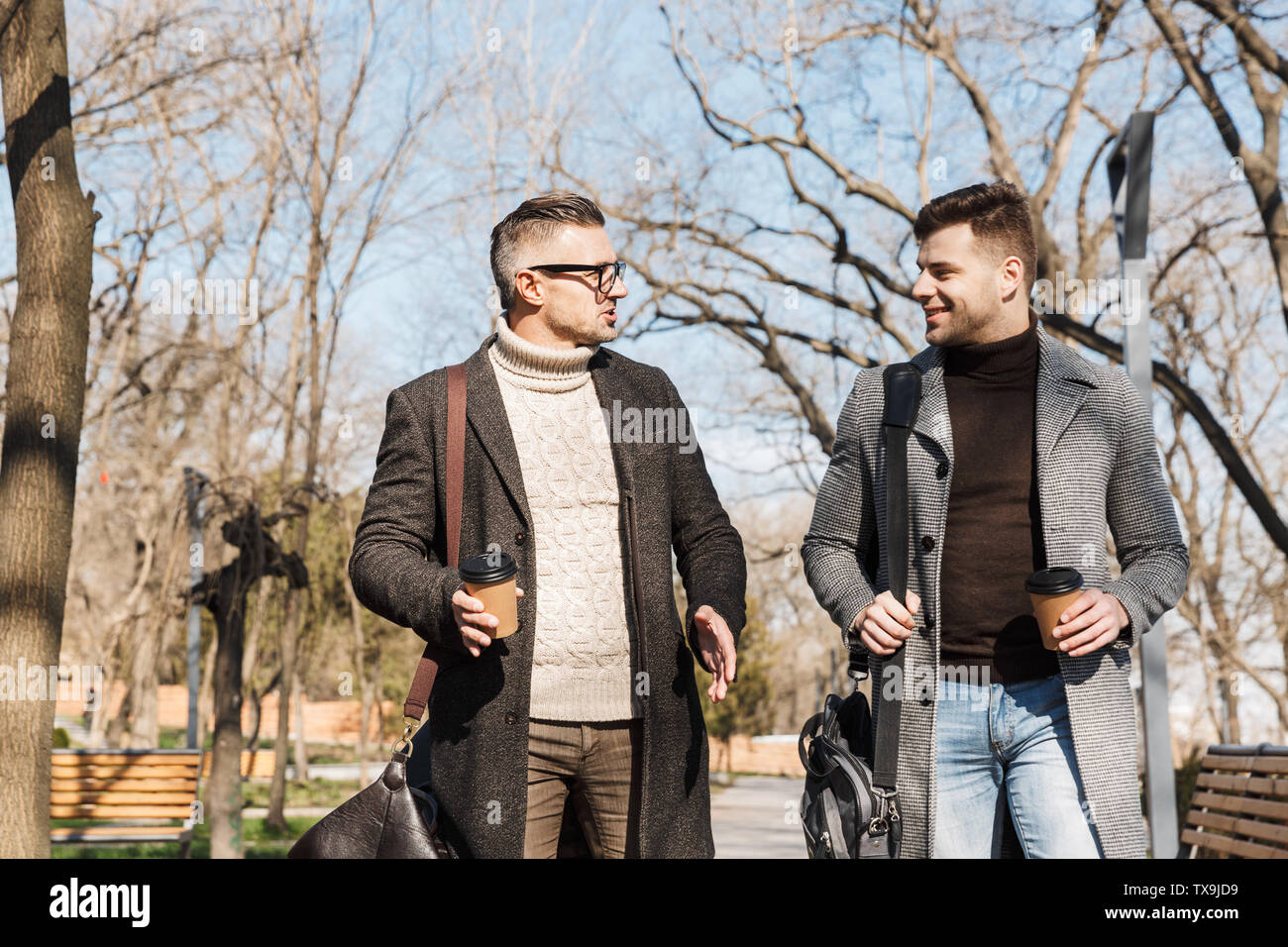 Two handsome men wearing coats spending time outdoors, drinking ...