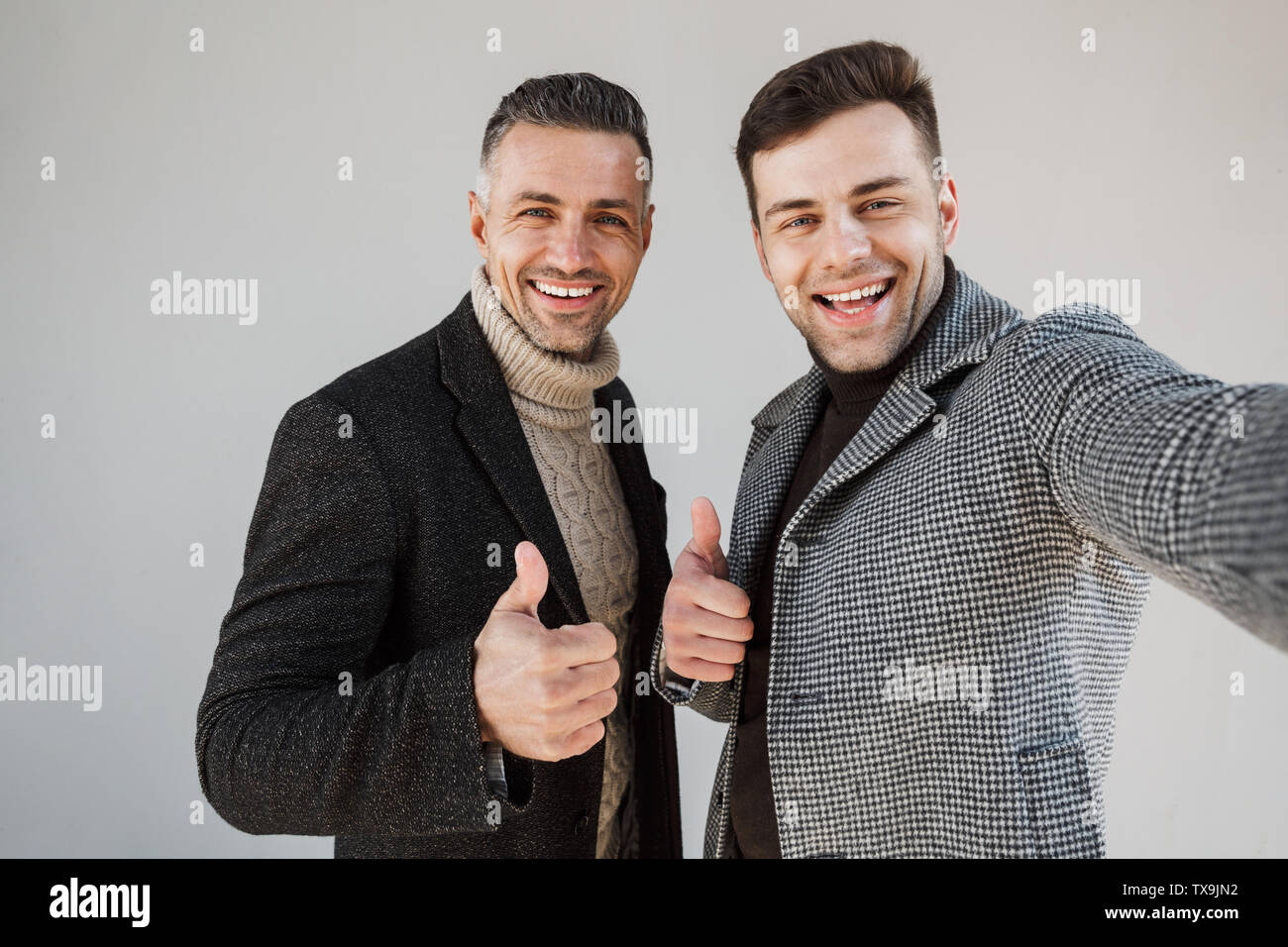 Two handsome men wearing coats over gray background, taking a selfie ...